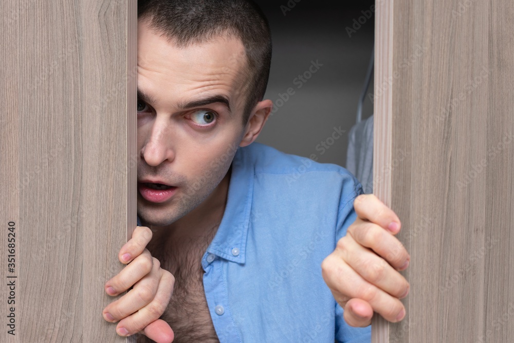 Unfaithful husband hiding in the closet with clothing, afraid of being ...