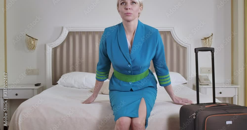 Elegant Caucasian woman in stewardess uniform with travel bag sitting ...