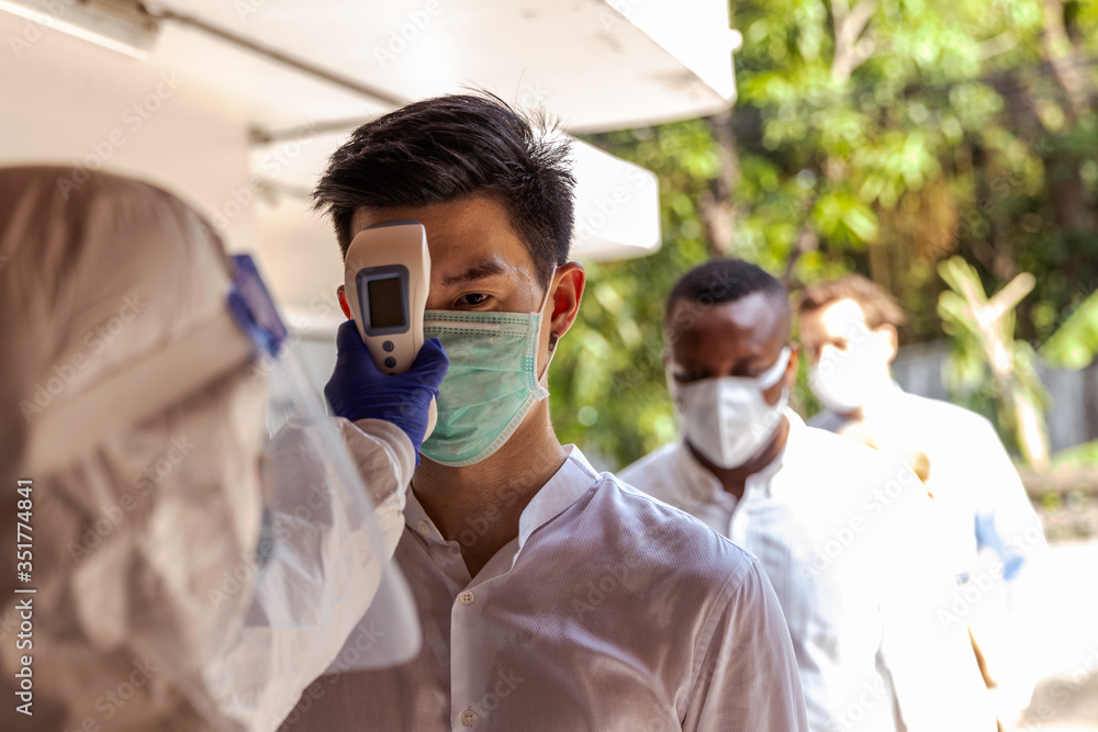 Office health controlling staff in PPE uses infrared thermometer device ...