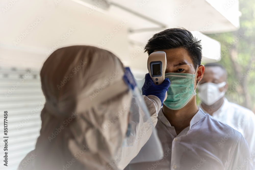 Office health controlling staff in PPE uses infrared thermometer device ...