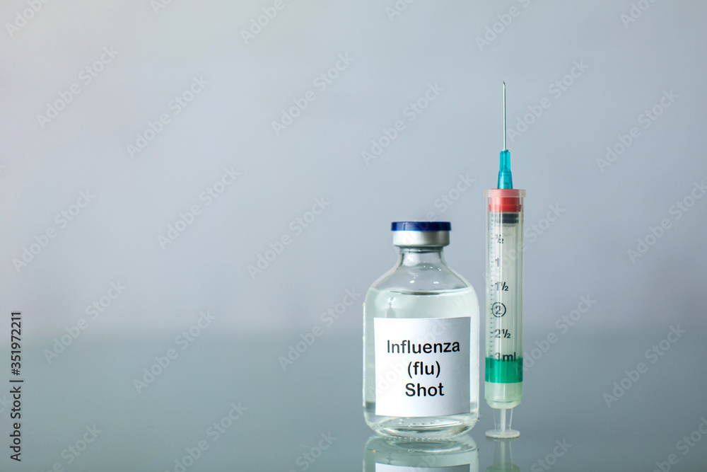 A bottle of a clear medicine influenza flu vaccine along with a syringe ...