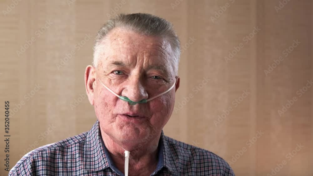 Old man with nasal cannula is watching in the camera and speaking. The ...