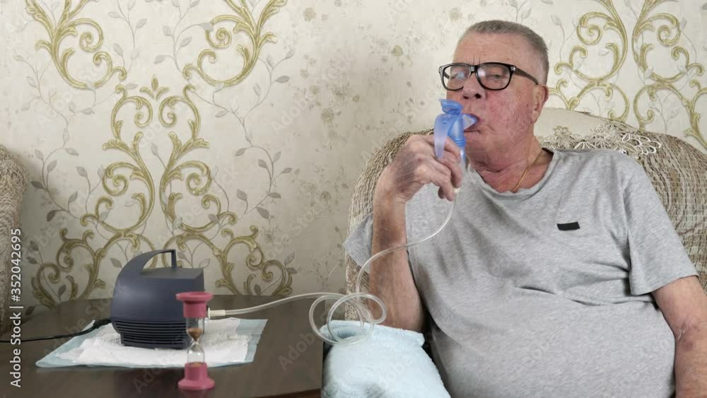 Old man in glasses is sitting near table and using inhaler. Man with ...