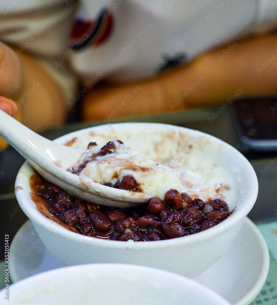 Spoons up Hong Kong red bean double skin milk pudding from a white bowl ...