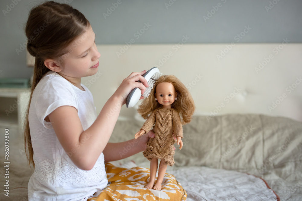 Caucasian girl combing a doll with long hair, a girl playing dolls ...