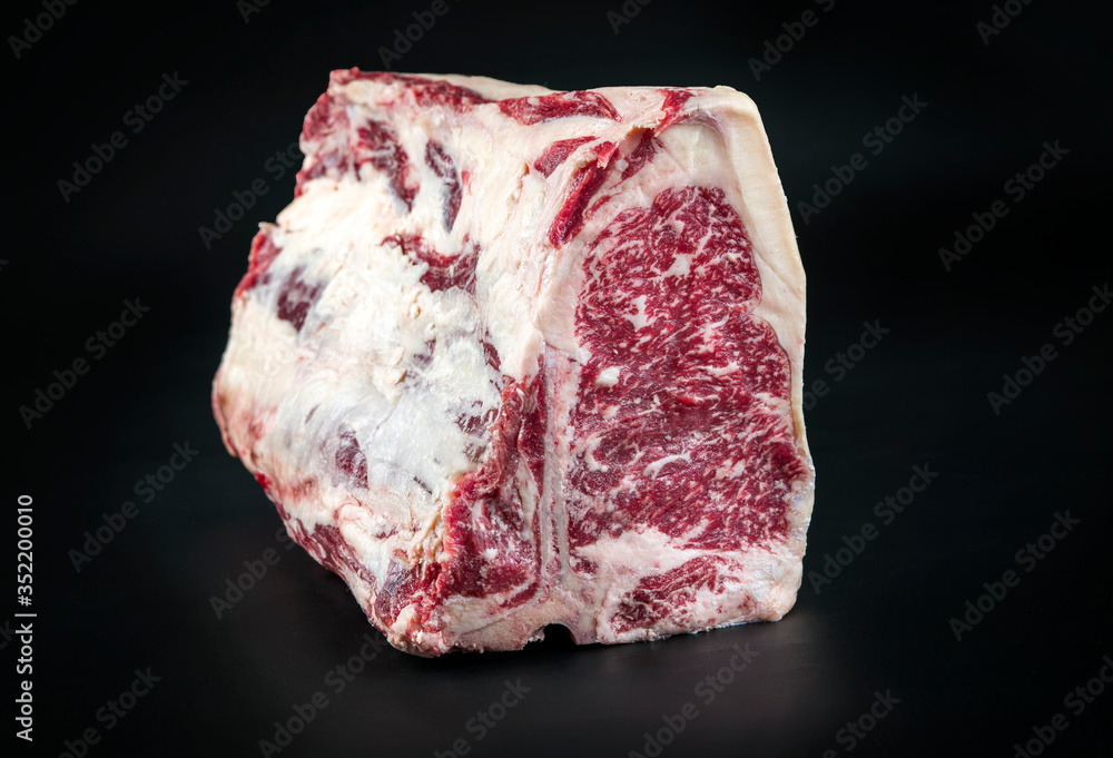 Raw dry aged wagyu porterhouse beef block offered as closeup on black ...