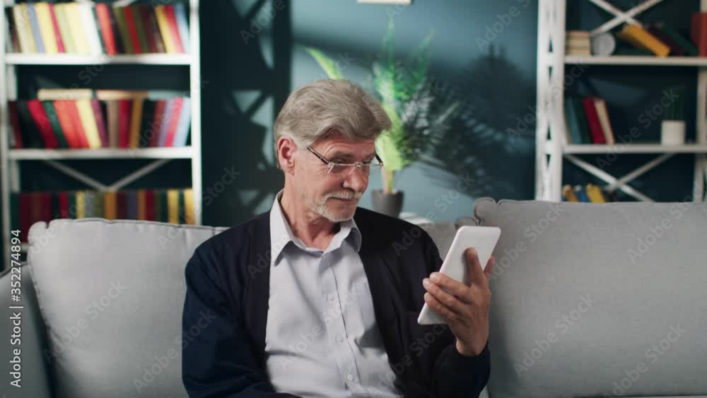 An elderly man in glasses is talking over the tablet and nodding his ...