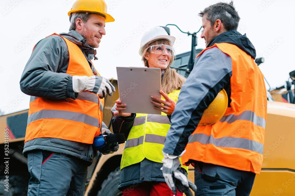 Three workers in a quarry discussing in front of heavy machinery Stock ...