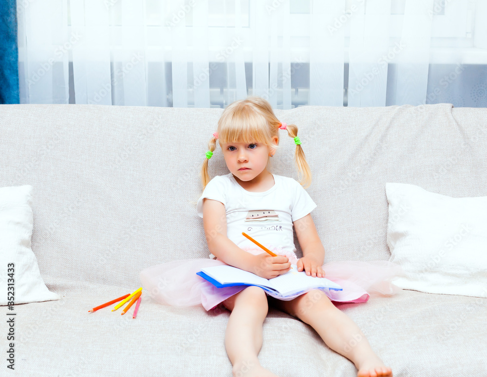 Foto de happy little girl with blond hair draws in a notebook at home ...