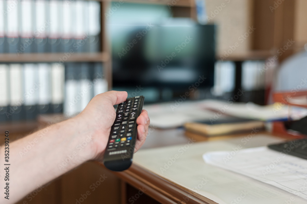 Remote control in a man's hand against the background of an office ...