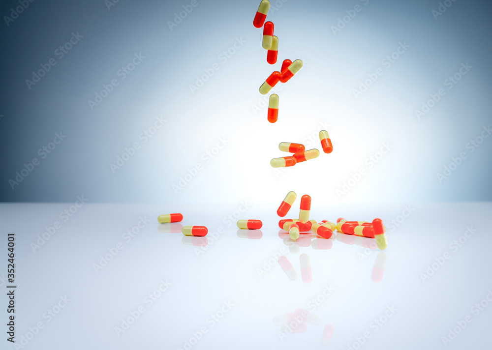 Yellow-orange capsules pill falling down on white table. Pharmaceutical ...