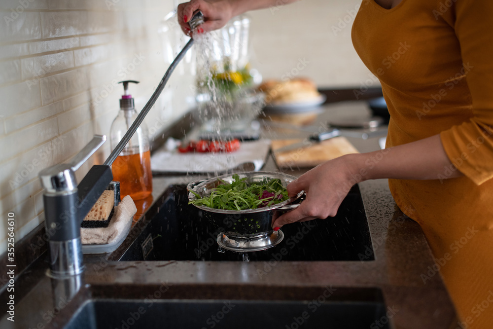 Girl washes the ingredients for the salad in the sink. Careful hygiene ...