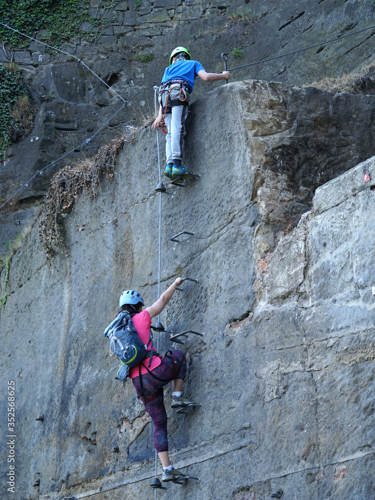 Mother with young son climbing steep ladder on via ferrata route ...