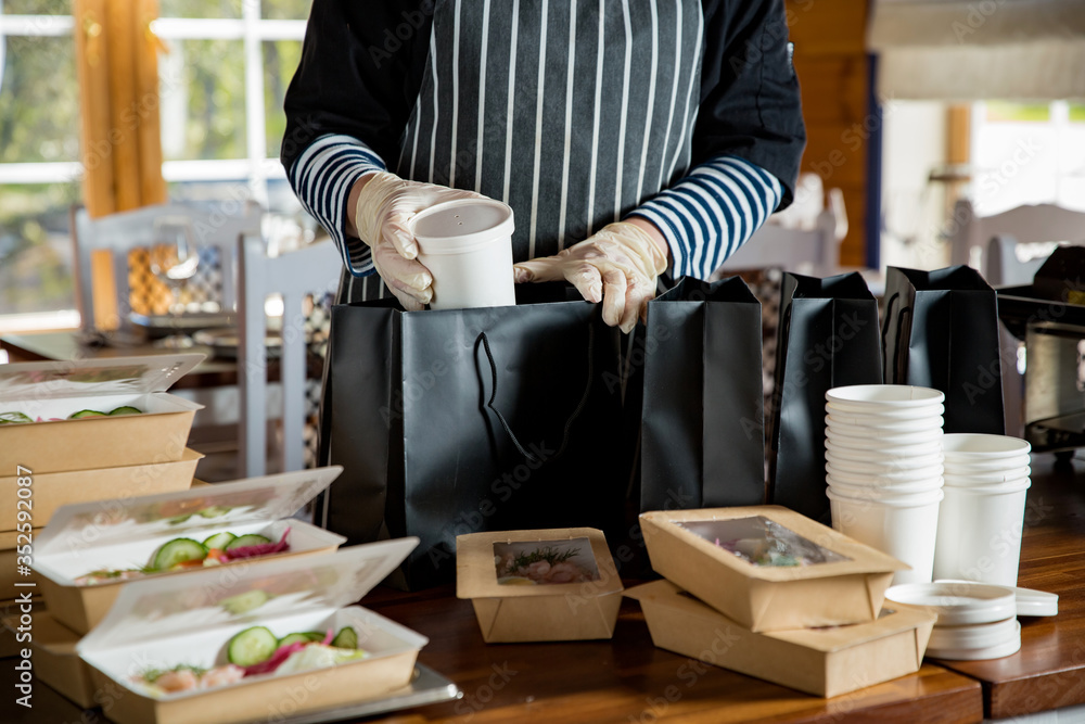 Restaurant worker wearing protective mask and gloves packing food boxed ...