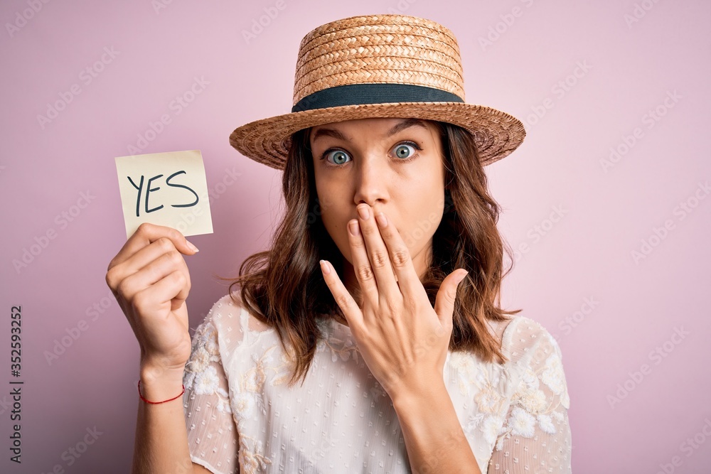 Young blonde girl wearing a hat holding paper note with yes word as ...