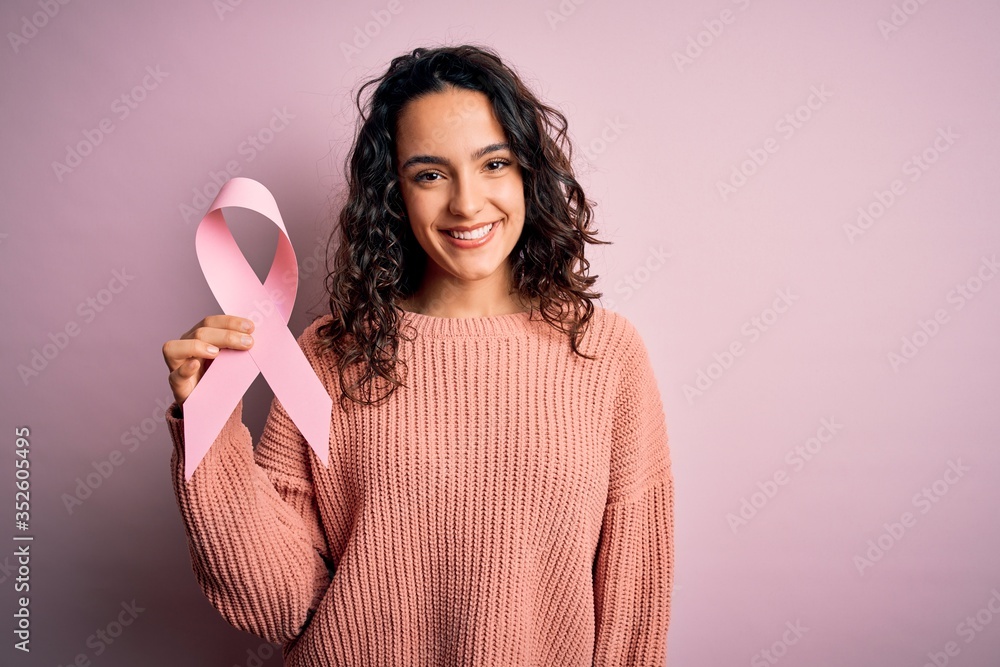 Beautiful woman with curly hair holding pink cancer ribbon symbol over ...