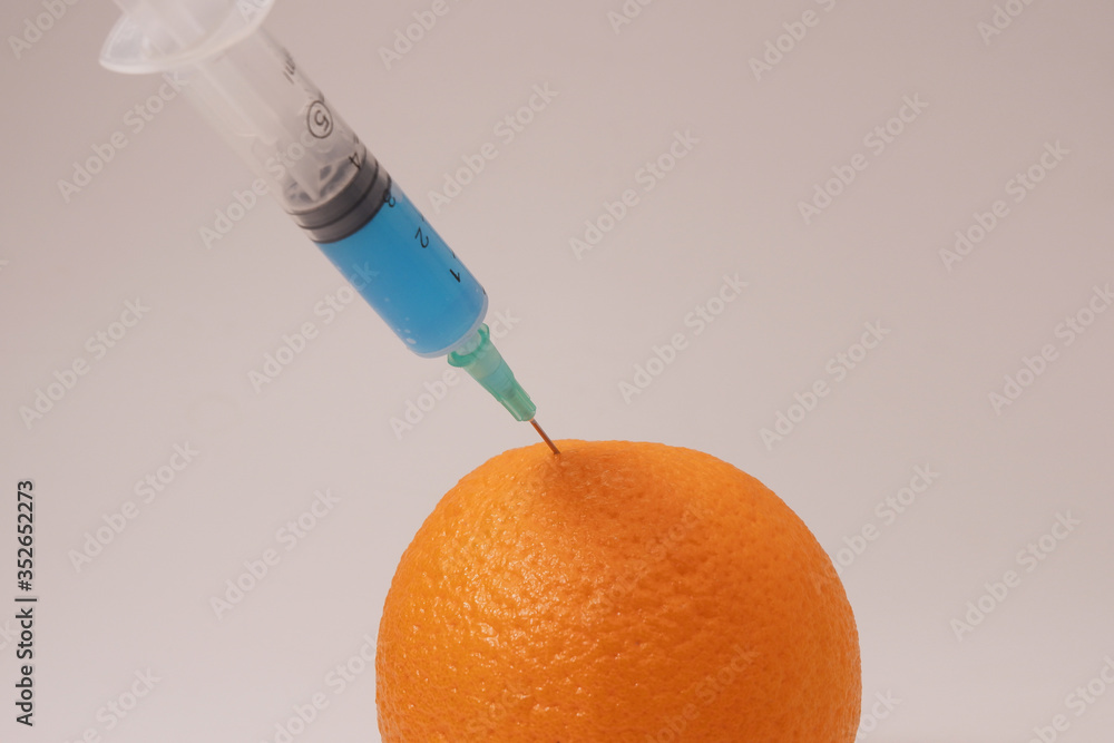 Injecting blue liquid into an orange fruit. Syringes for injection ...