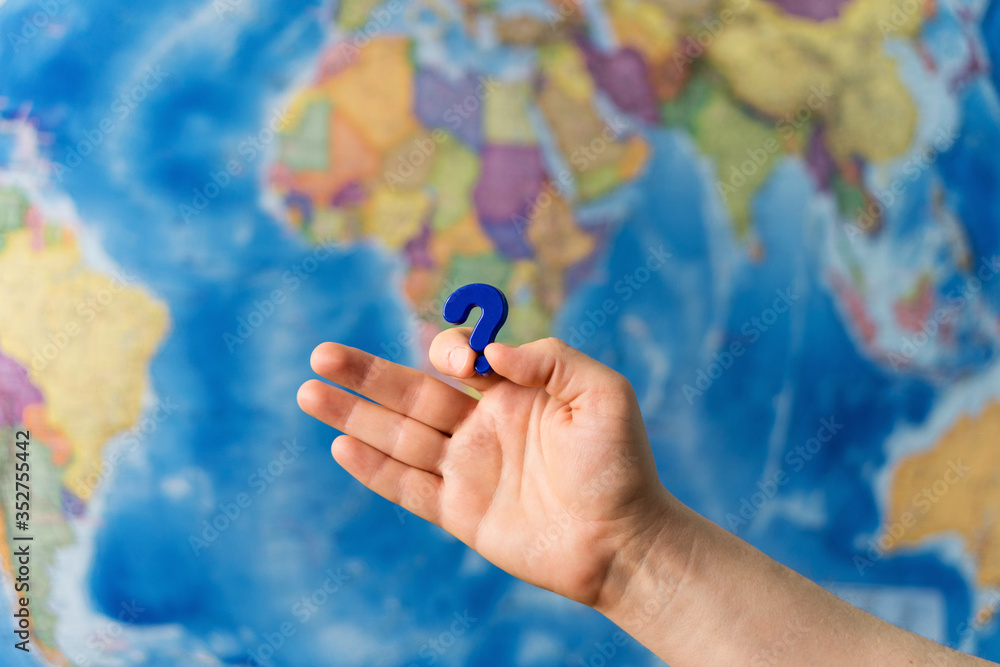 Adult hand holding question mark plastic toy on the world political map ...