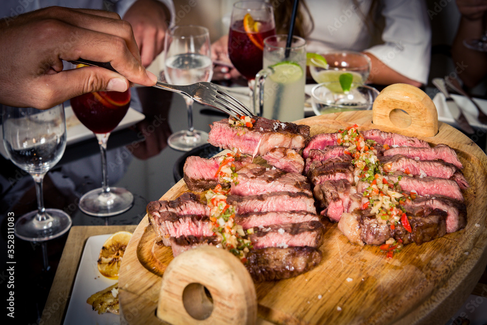 Cut juice steak on a table with friend sharing food, hand with fork ...