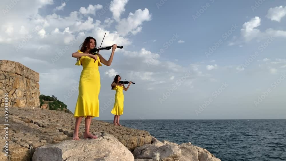 Two beautiful twin sisters violinists in yellow concert dresses are ...