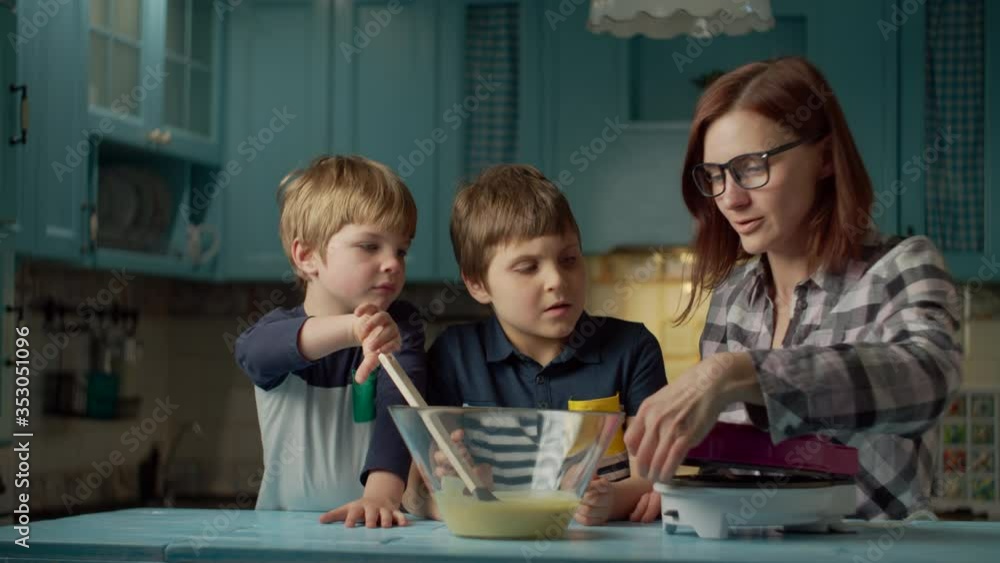 Young 30s mother with two kids making waffles in waffle maker at home ...