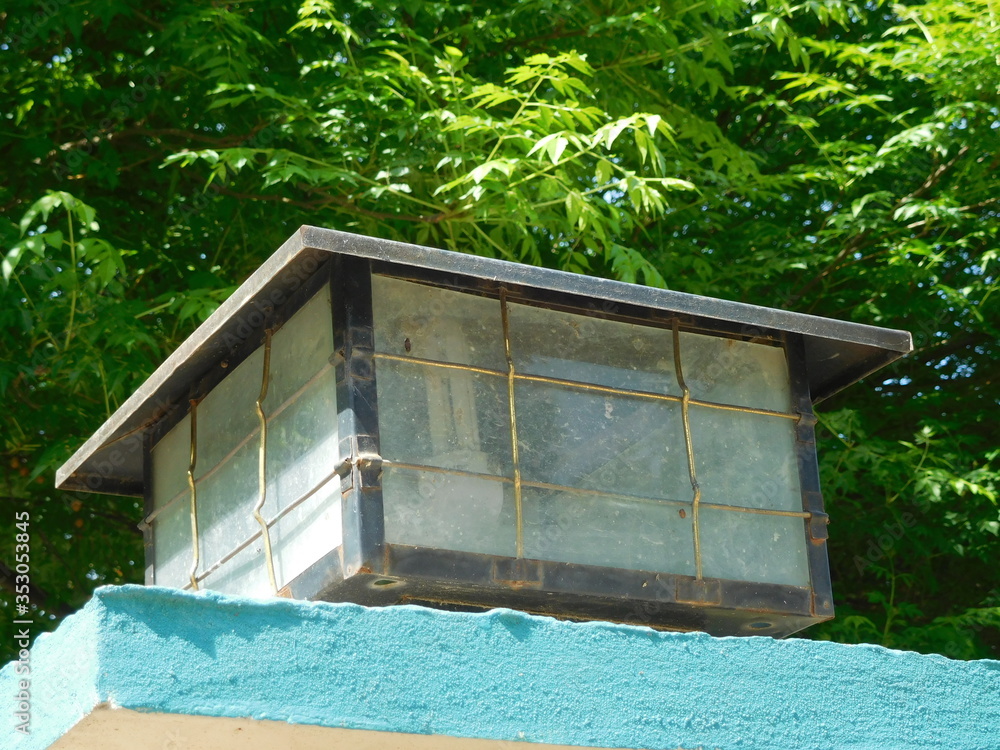 lamp with metallic cage on a pillar of gate or a fence post in day ...