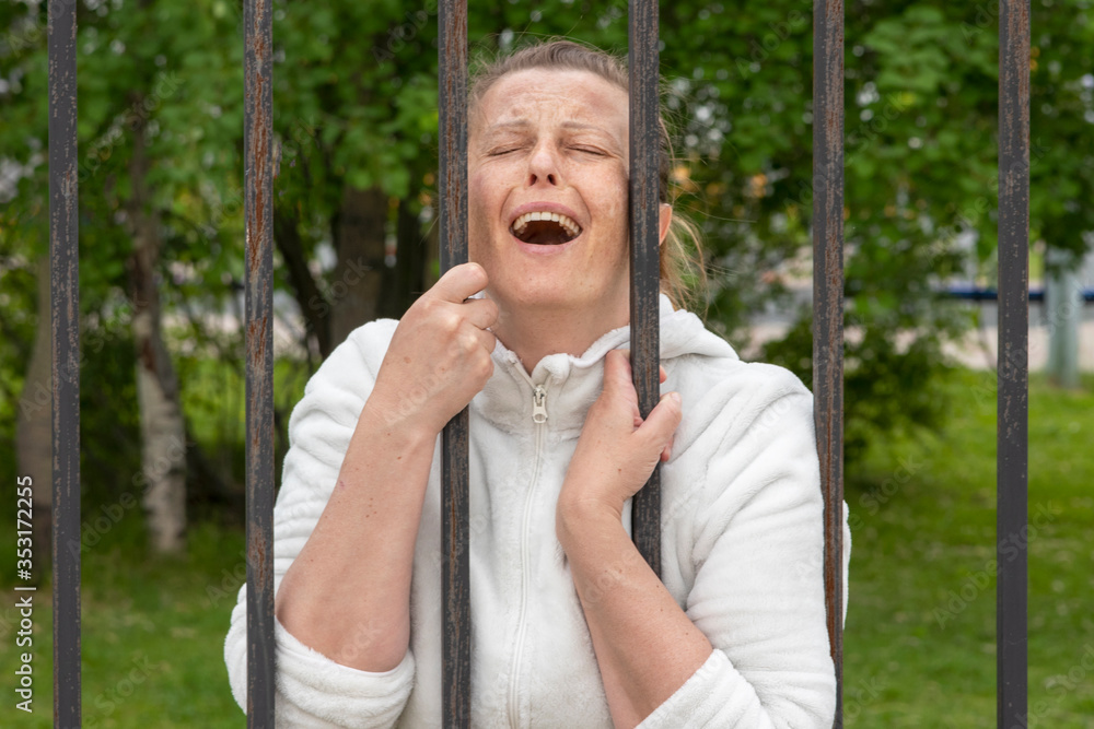 Emotional condition. A woman behind an iron fence, her hands clutching ...