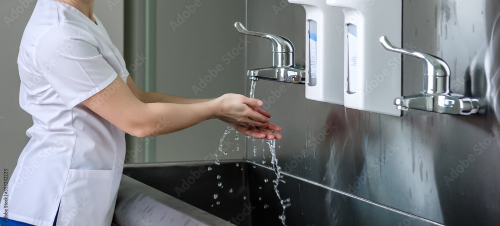 The doctor washes his hands under the tap in a stainless steel sink ...