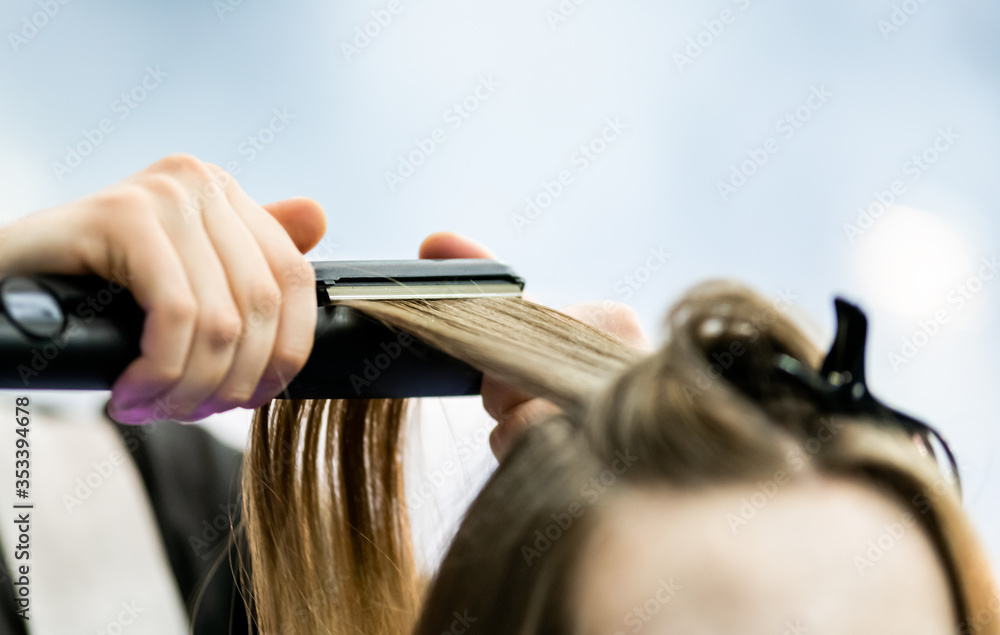 Poster Professional hairdresser straightening long blond hair using ...