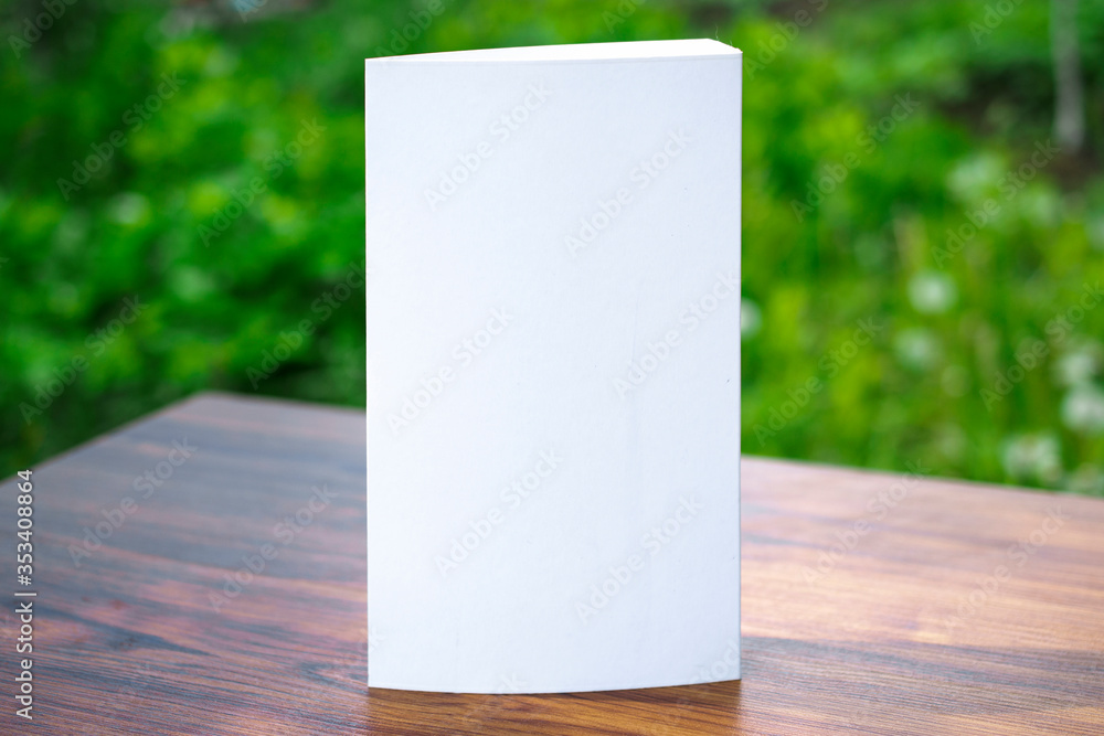 Blank vertical paper table tent on a wooden table with blurred green ...