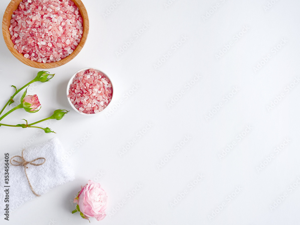Spa flatlay composition. Sea salt in wooden jar, towel, flower on white background. Top view ...