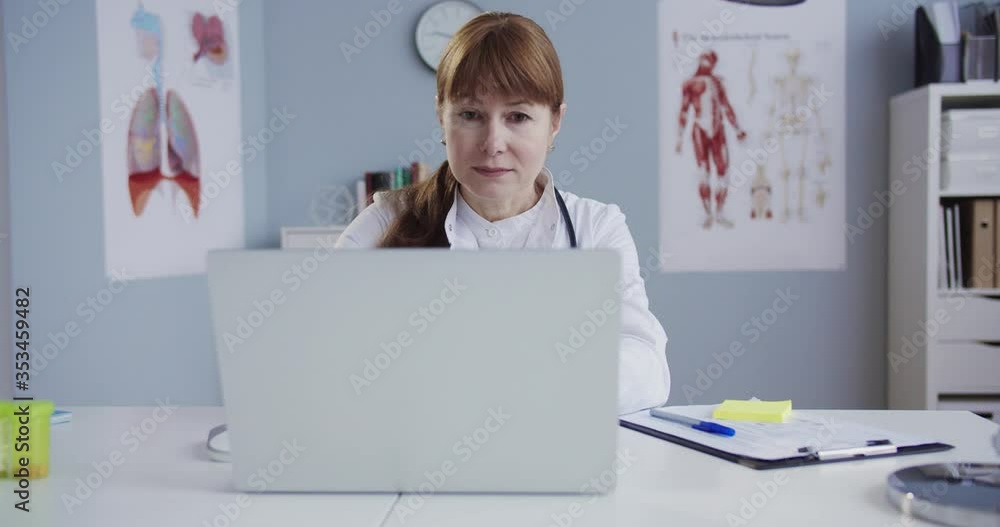 Beautiful female medical practitioner typing on laptop in white gown at ...