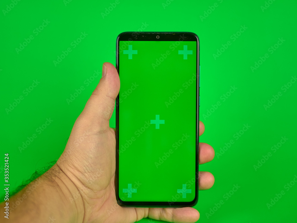 Fotka „Man's hand holding a mobile phone with a vertical green screen, chroma key smartphone ...