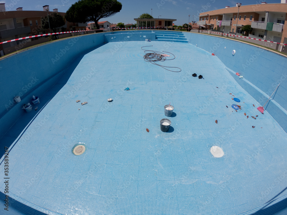 Empty swimming pool with broken tiles with metal ladder waiting for ...