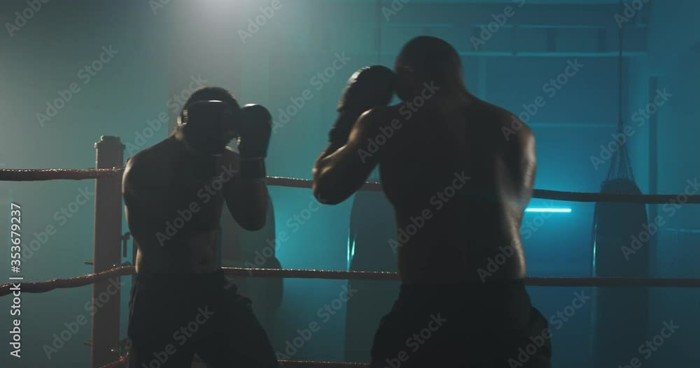 Two Caucasian silhouettes of boxers fighting at ring in darkness ...