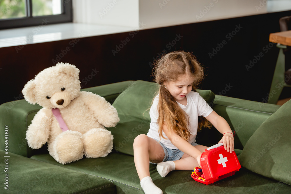 cute child touching toy first aid kit box near teddy bear while playing ...