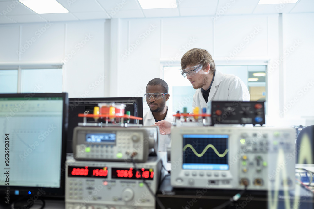 Two students wearing lab coats and eyeglasses in a laboratory with ...