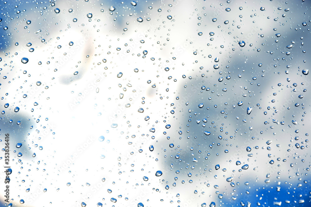 Raindrops on the transparent window pane, against a blurry blue sky ...