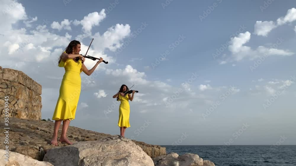 Two beautiful twin sisters violinists in yellow concert dresses are ...