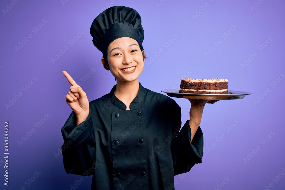 Young chinese chef woman wearing cooker uniform and hat holding tray ...