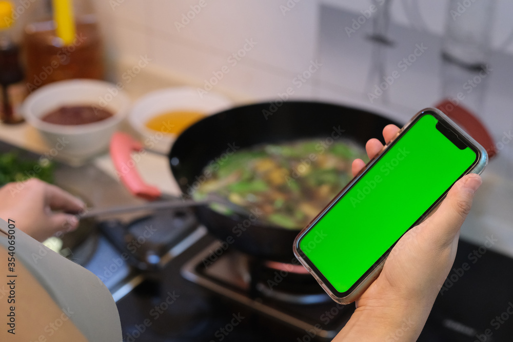 over shoulder of woman using green screen smartphone while cooking in ...