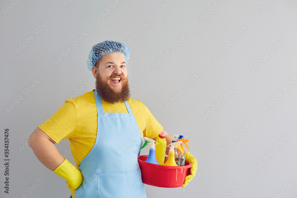 Funny fat man with a beard in an apron cleans up on a gray background ...