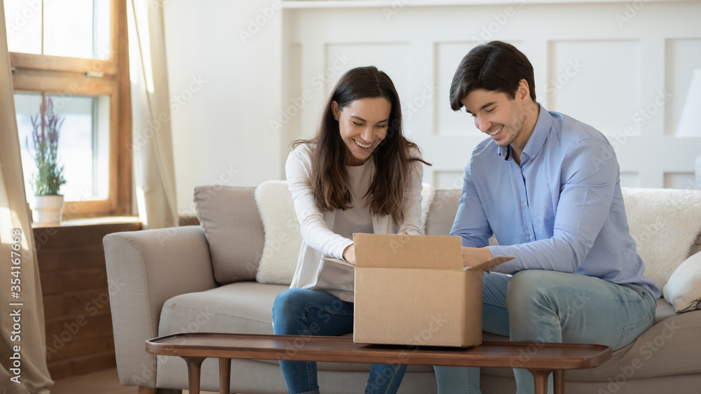 Happy young caucasian couple sit on sofa at home feel excited unpacking ...