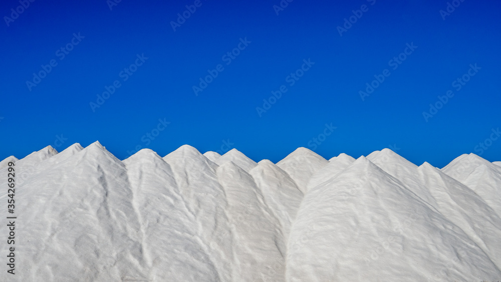 huge white hills of dried clean sea salt in front of clear blue sky and ...