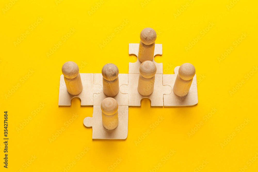 Wooden figures on puzzles on yellow background as a symbol of team ...