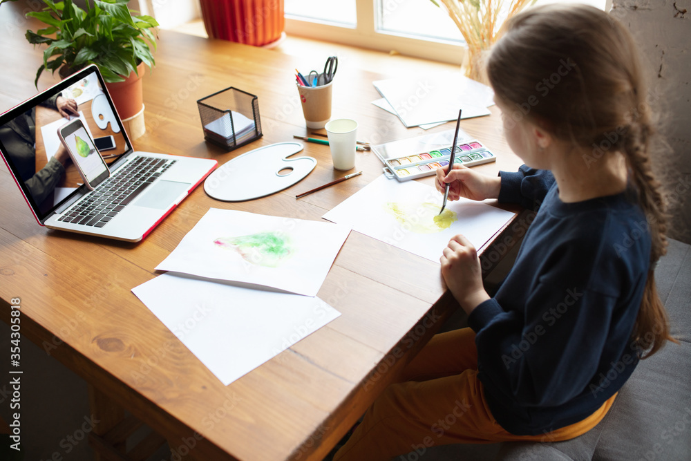 Girl drawing with paints and pencils at home, watching teacher's online ...