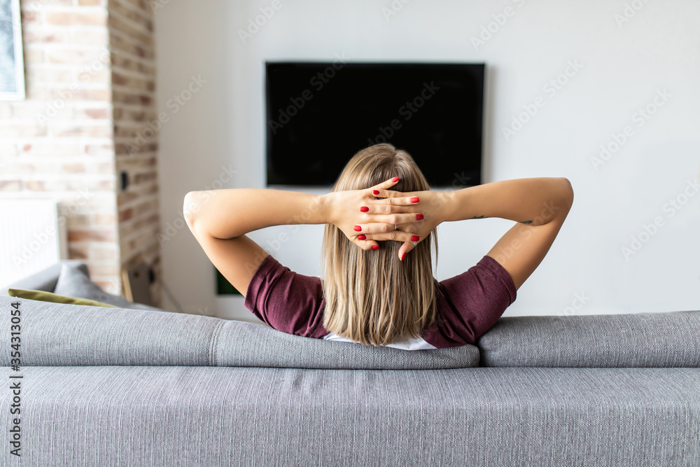 Back view of young woman sitting watching television program at home ...