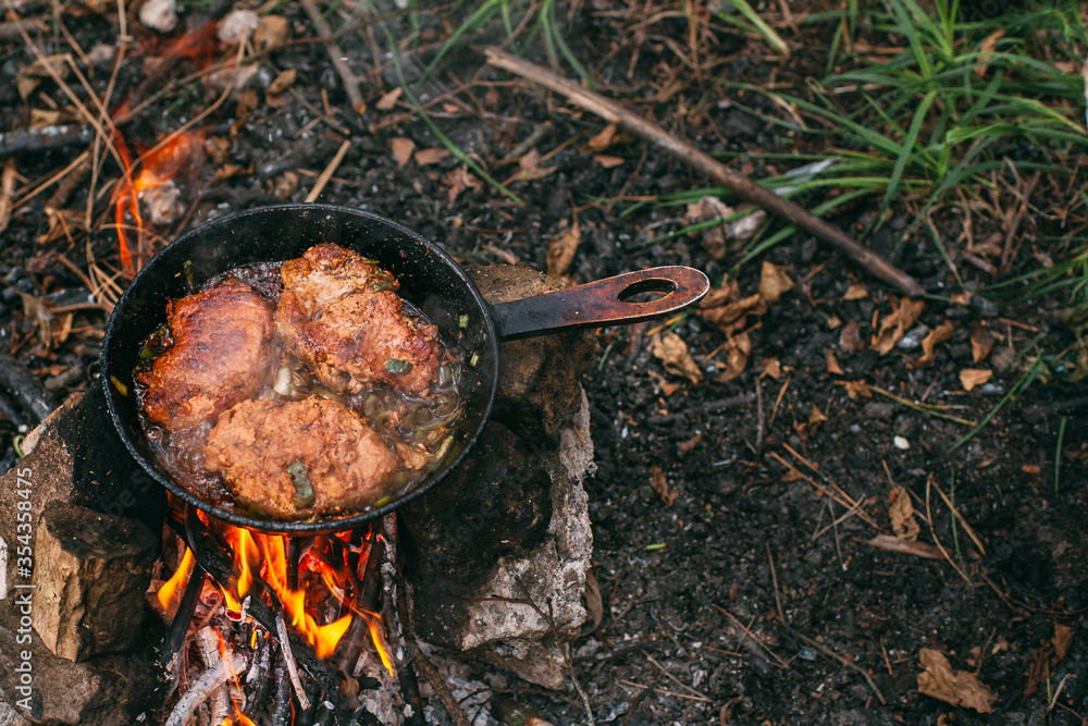 Frying meat in a pan over an open fire with leek. Steak in a pan on a ...