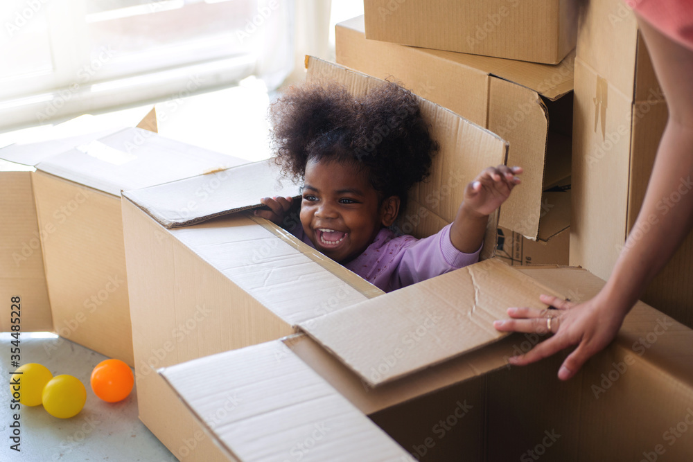 Dark skinned child girl playing in cardboard box in room, hiding in a ...