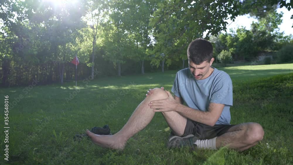 Male runner in pain on injury at the knee the leg on a park exercising ...
